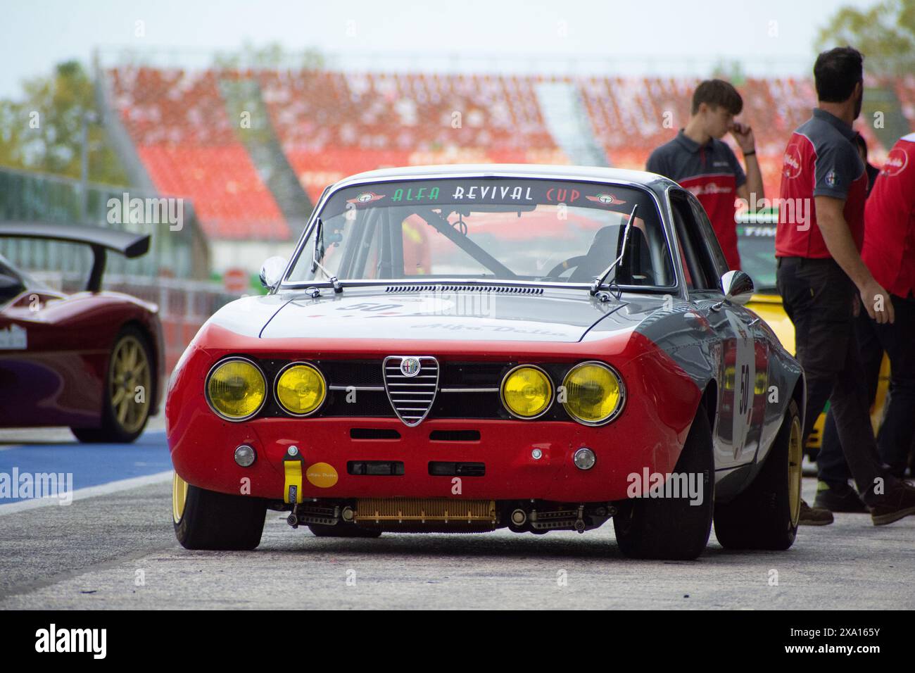 A group of men standing near a parked red car at a race track Stock ...