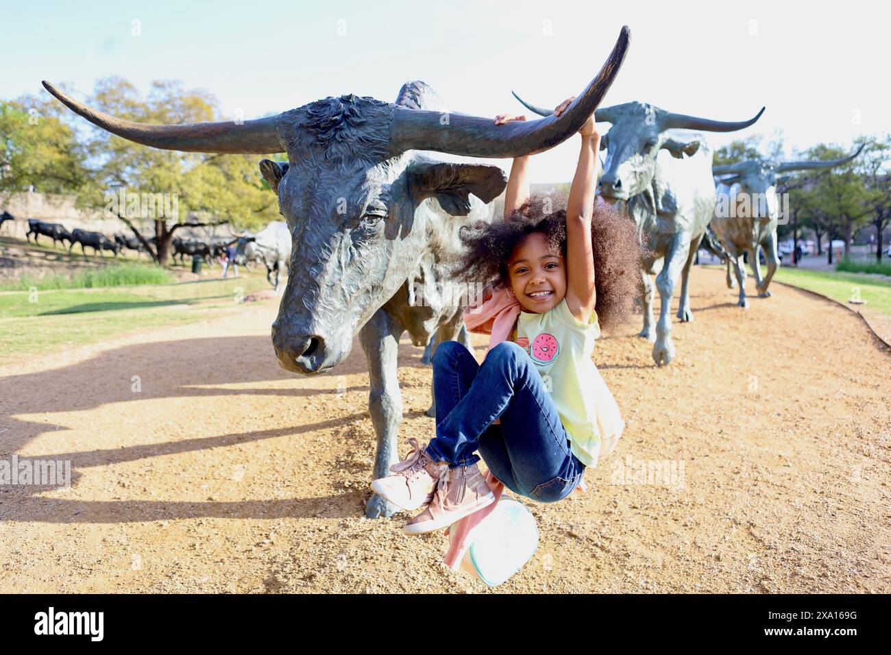 A happy young girl sitting under a bull statue Stock Photo - Alamy
