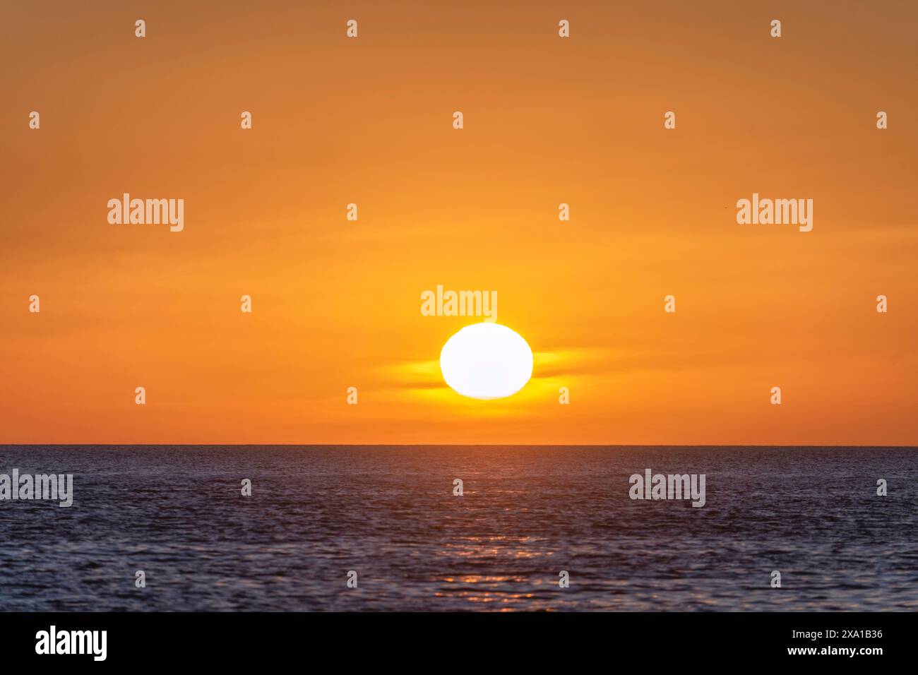 A large yellow sun casts its reflection upon the sea's surface, bathing ...