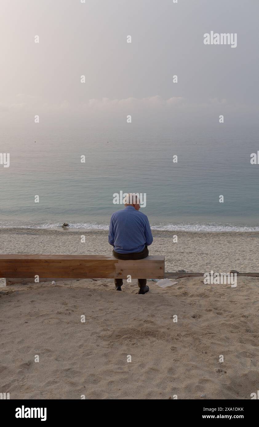 A man sitting on a beach bench with ocean waves in the background Stock ...