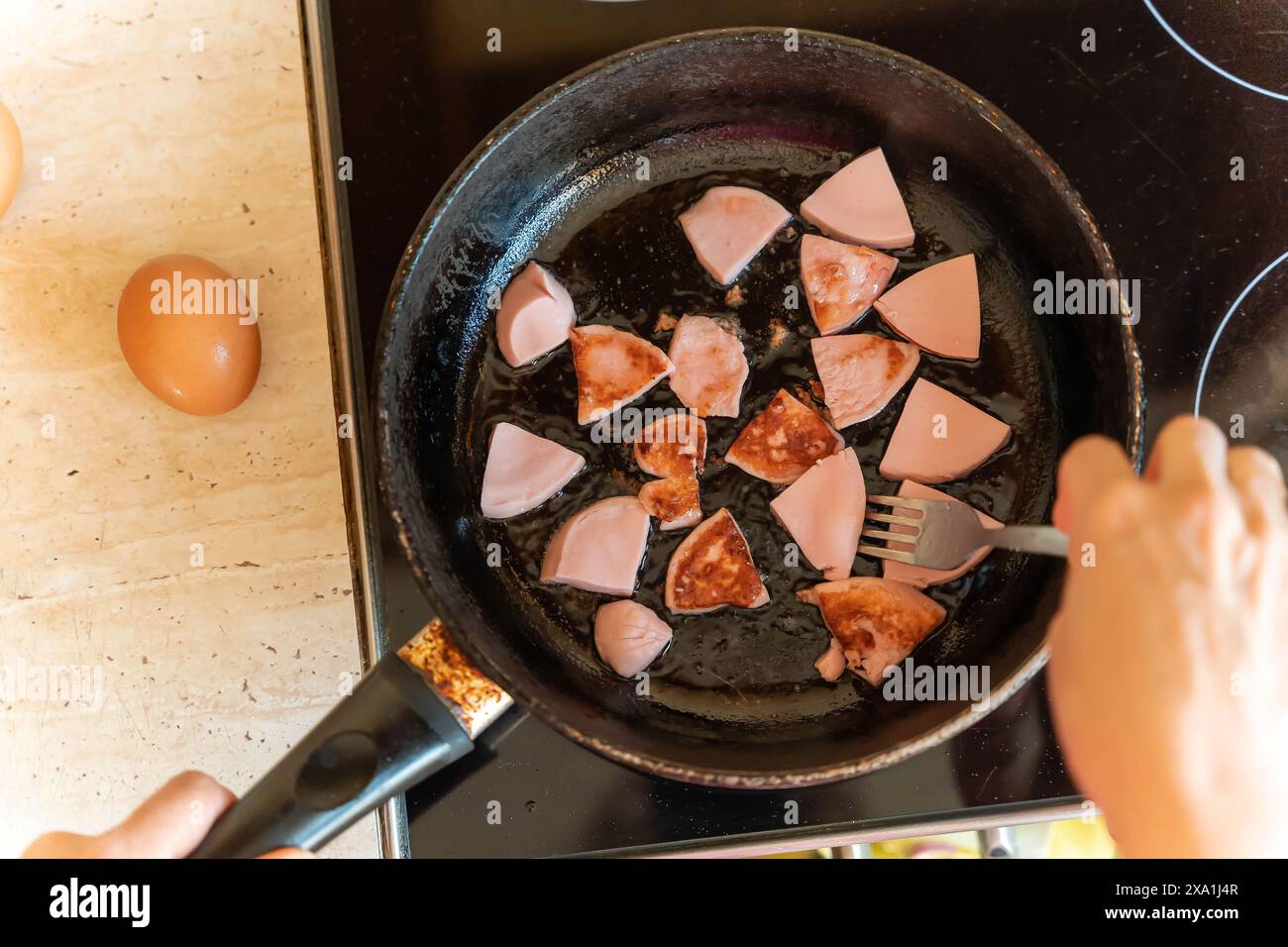 Close-up overhead view of sausage slices frying in a pan on the stove ...