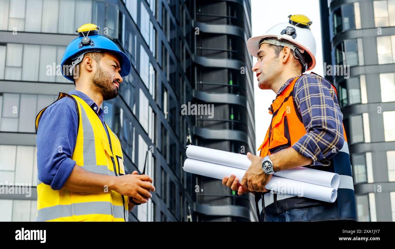 The two engineers in safety gear, hard hats, and holding a blueprint ...