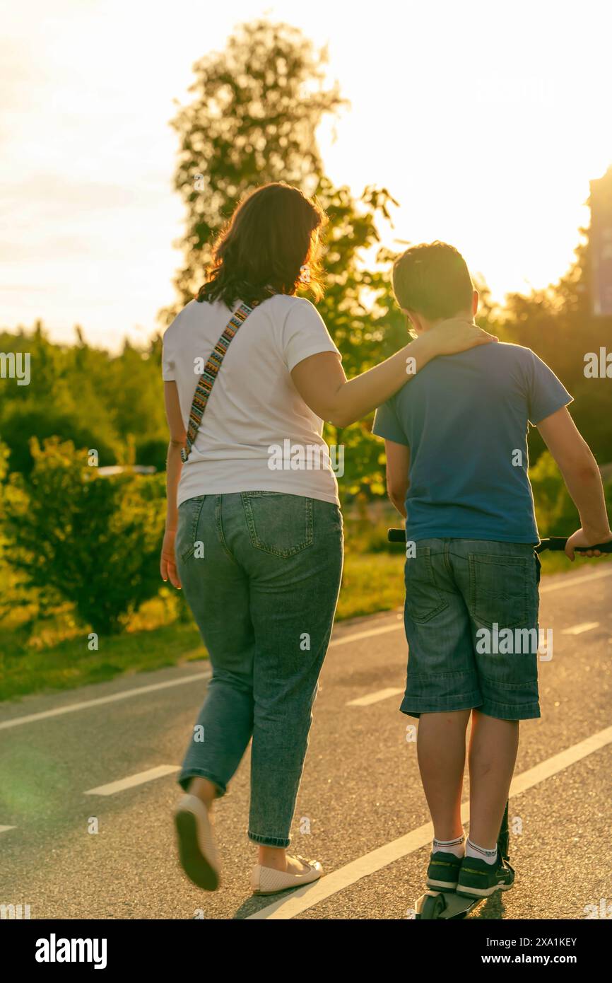 Mom and son walk on a paved path, with the sun shining warmly overhead ...