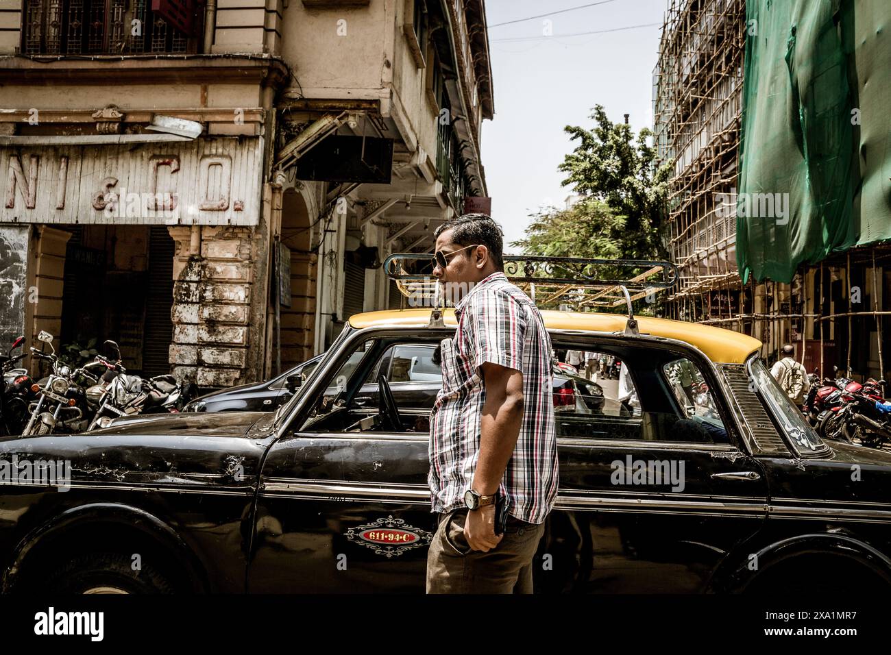 A man in front of a black taxi parked by urban buildings in Mumbai ...