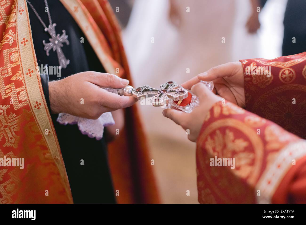 The priest in a red and gold robe holding a cross during a traditional Armenian wedding ceremony ...