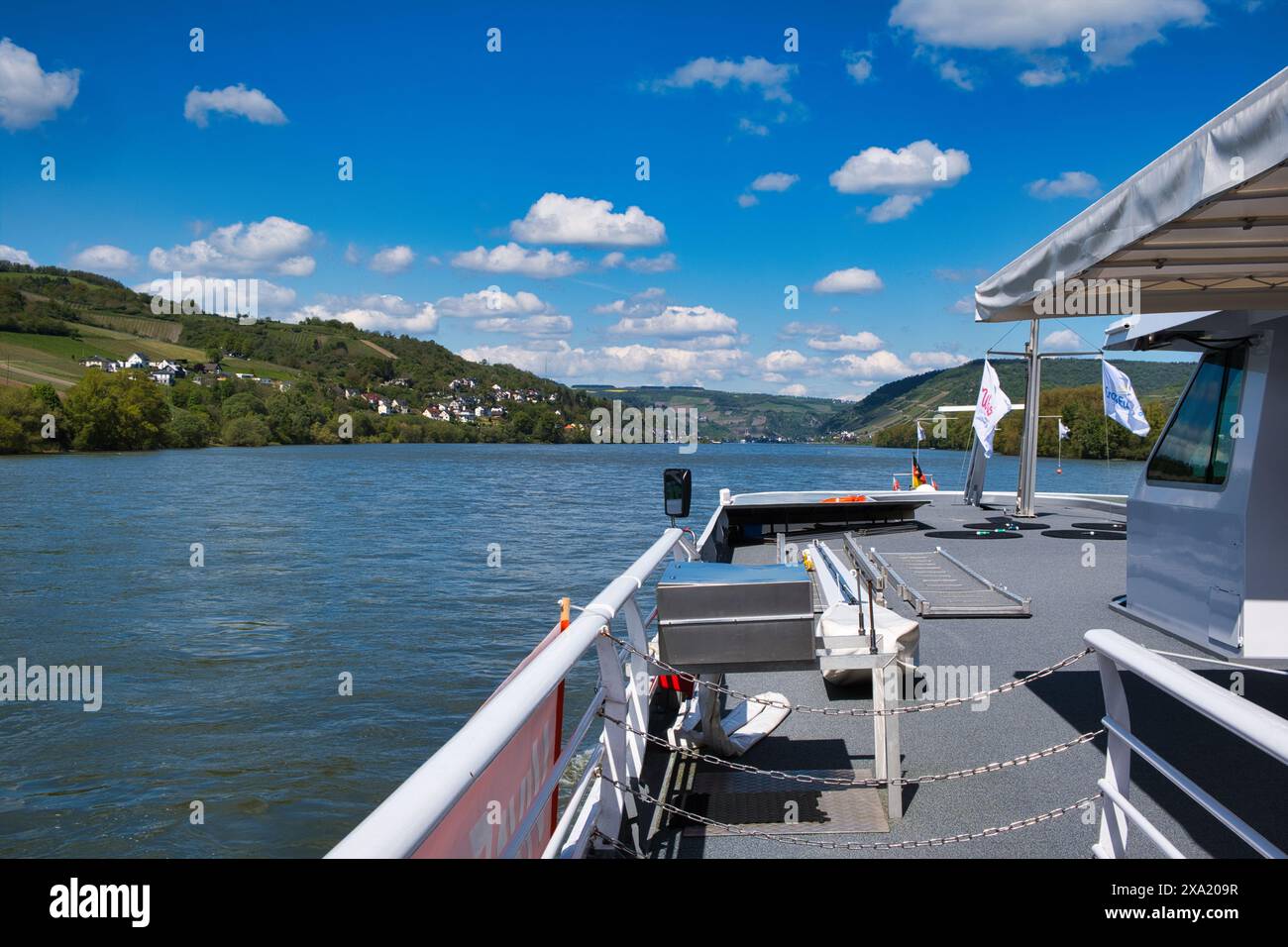 A long boat with front and side decks lowered, floating on a river ...