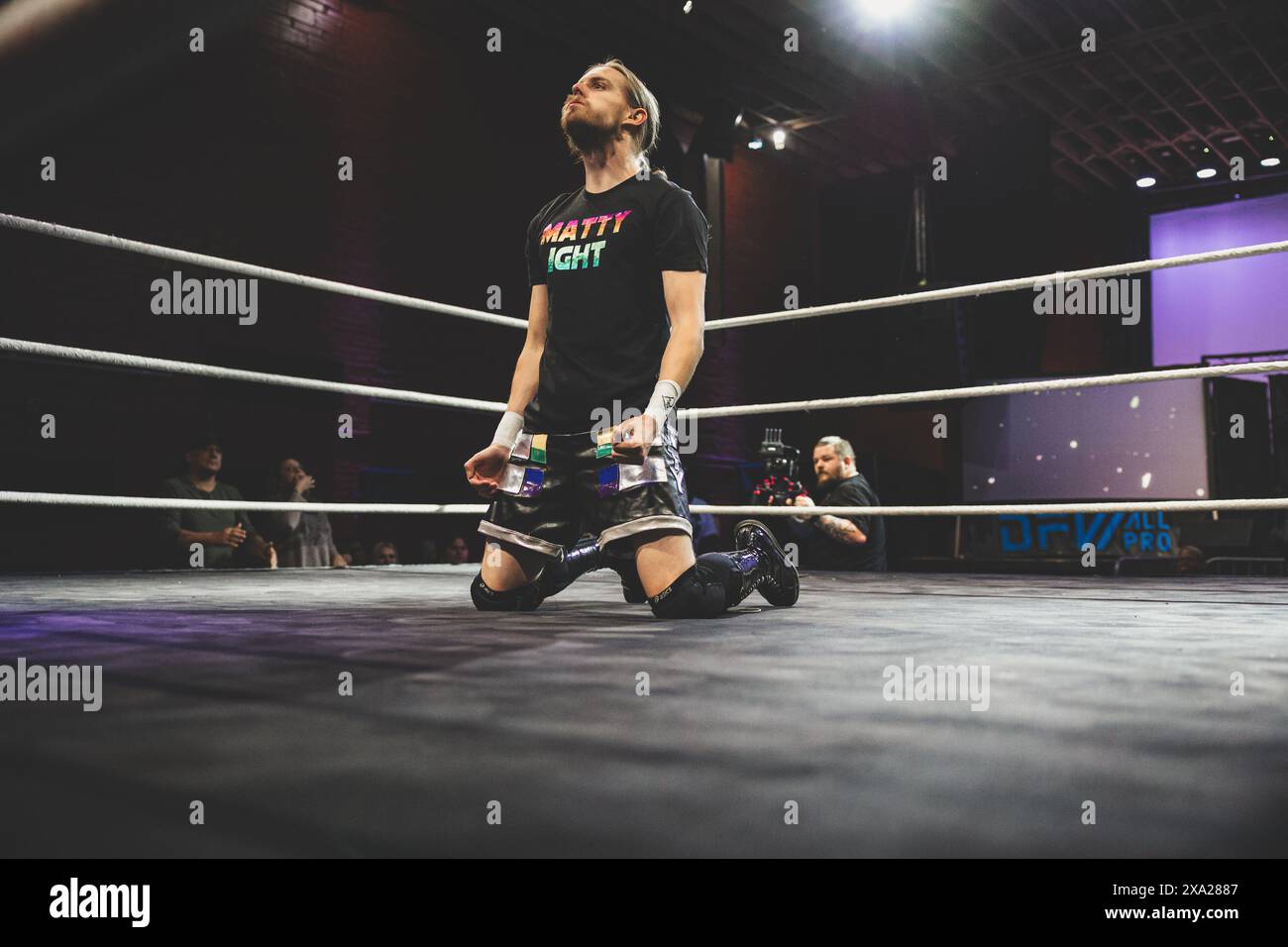 Pro Wrestler kneels in ring, opponent watches from the corner out of ...