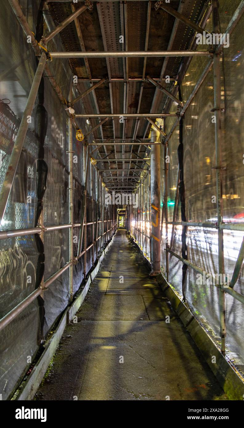 Protected scaffolding covered sidewalk illuminated by headlights at ...