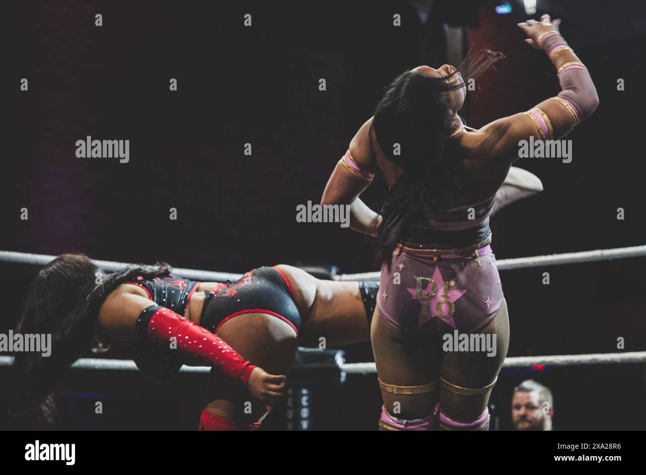 A female wrestler executing a stunt in the ring as a spectator observes ...