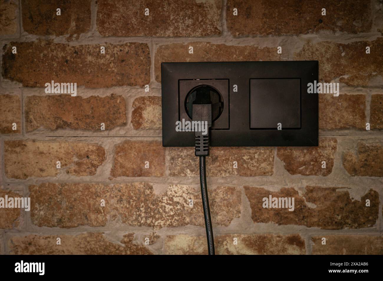 A close-up image of a black electrical outlet mounted on a brick wall ...