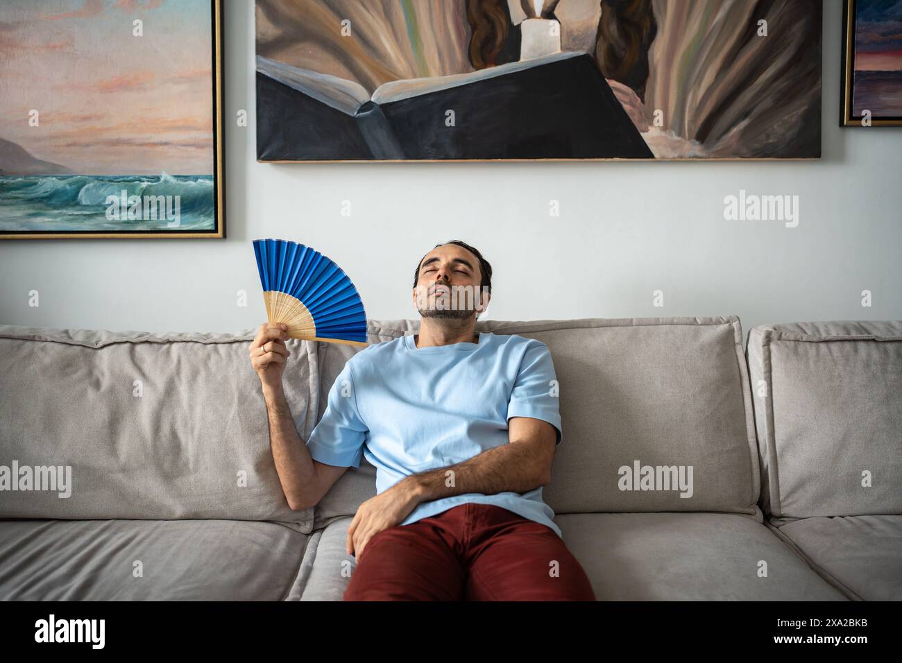 Exhausted unhappy man blowing with paper fan, suffering from stuffiness ...