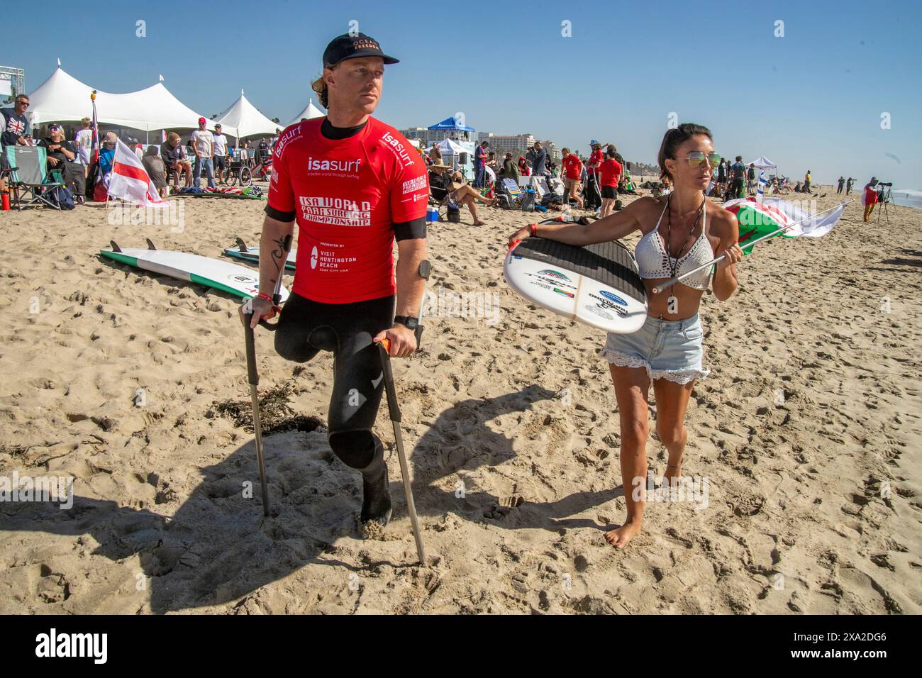 A parasurfer amputee uses crutches while a companion carries his ...