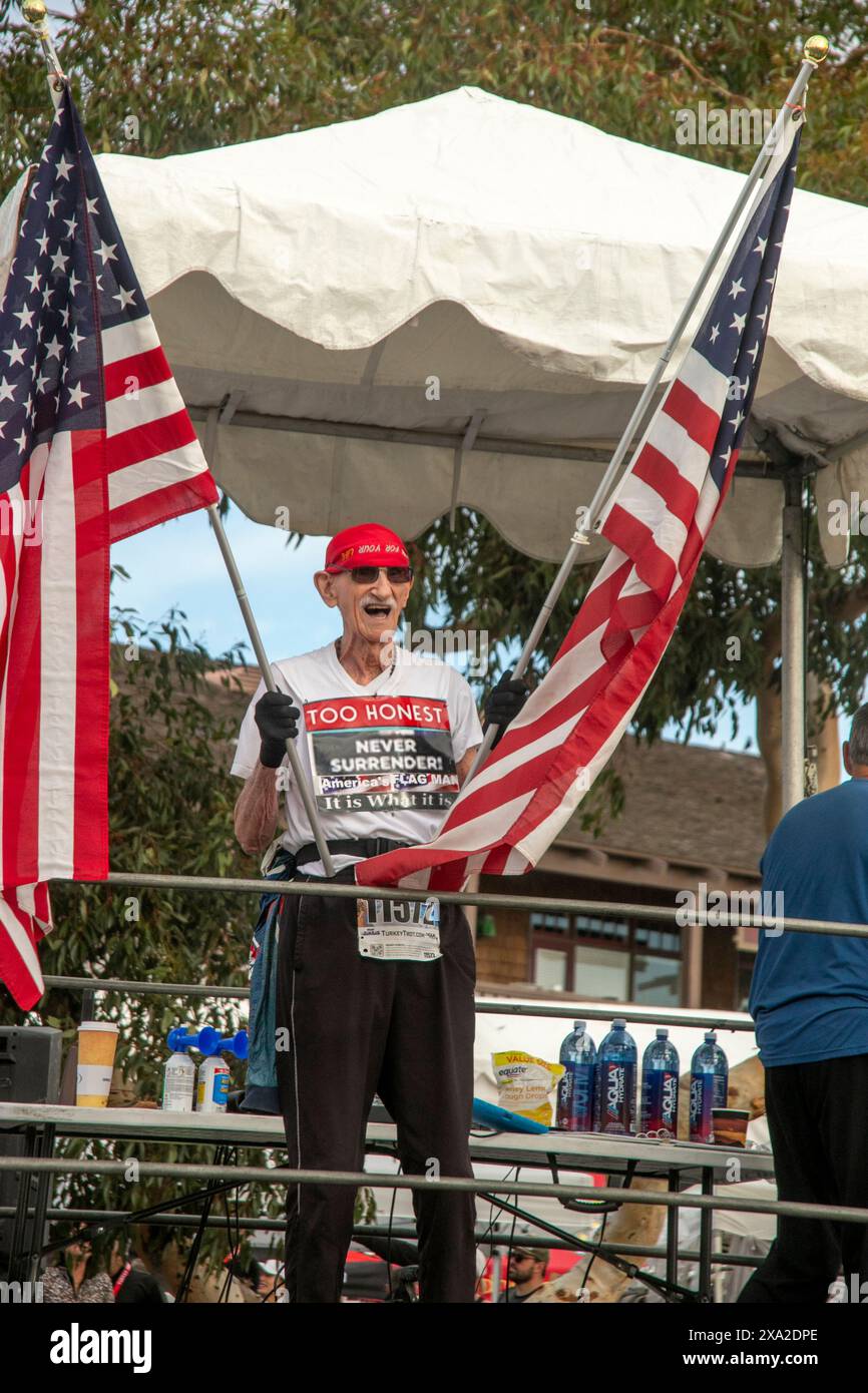 A 90-year-old man waves two US flags at a Thanksgiving day festival in Dana Point, CA Stock ...