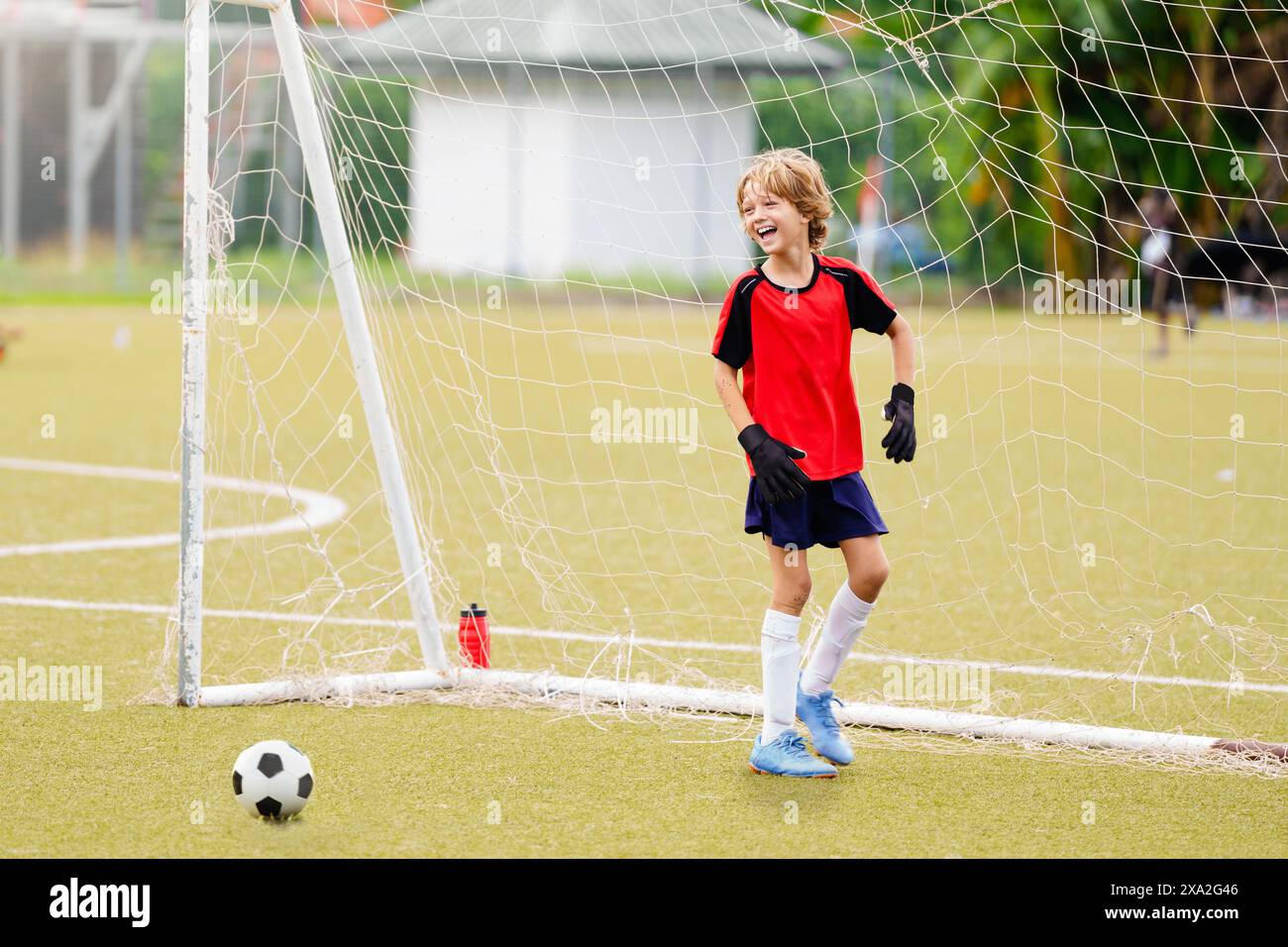 Kids play football on outdoor field. Little goalkeeper in goal ...
