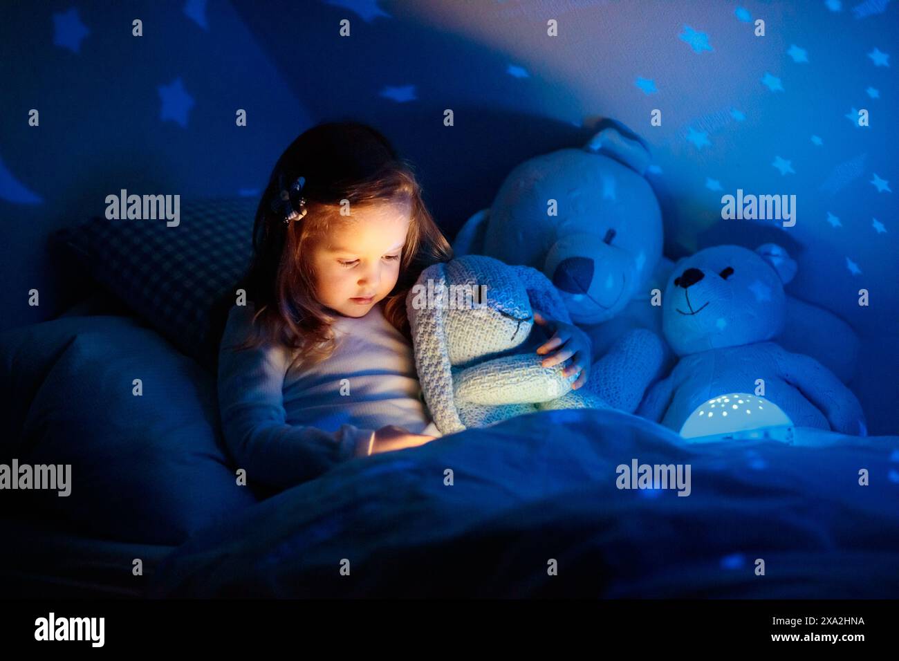 Little girl reading a book in bed. Dark bedroom with night light ...