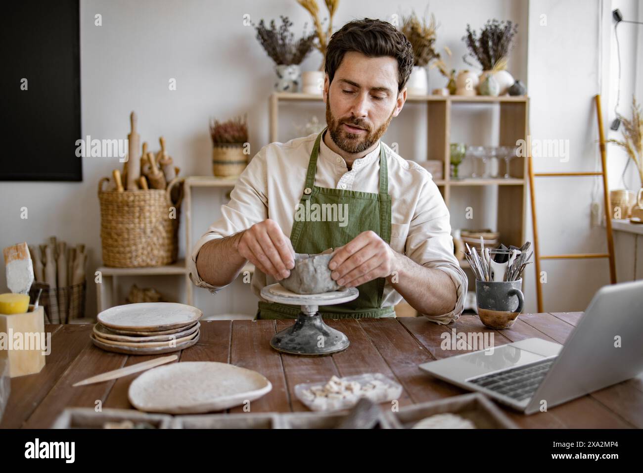 Male artist shaping clay pot in rustic studio filled with pottery tools ...
