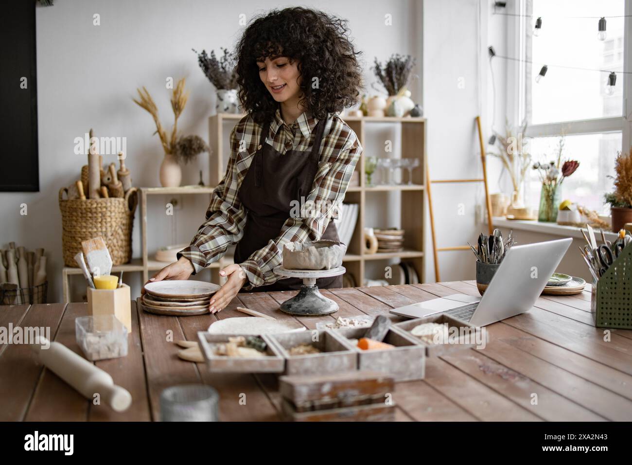 Young woman working in pottery studio organizing tools and materials ...