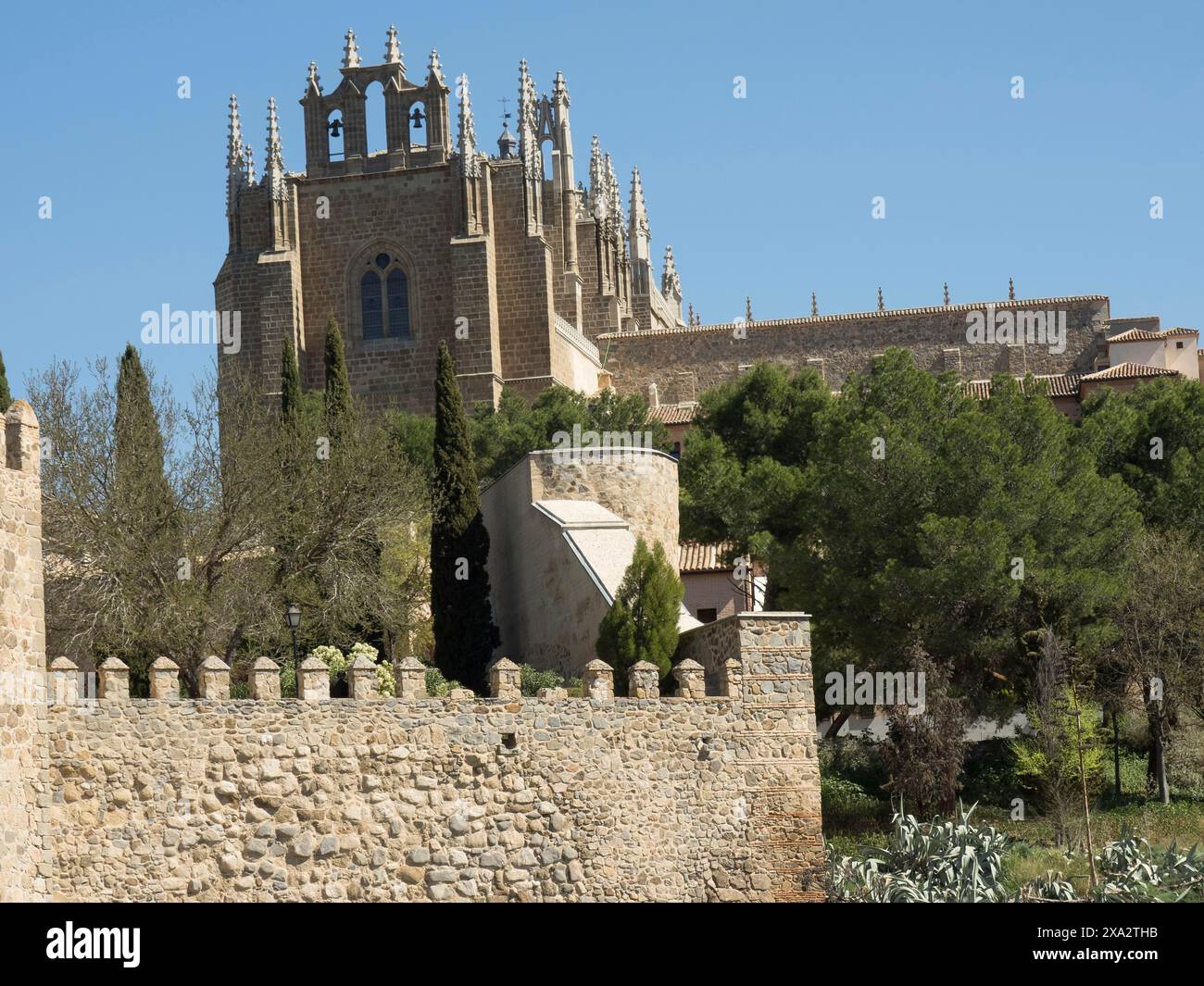 A Gothic monastery surrounded by dense trees and a historic stone wall ...
