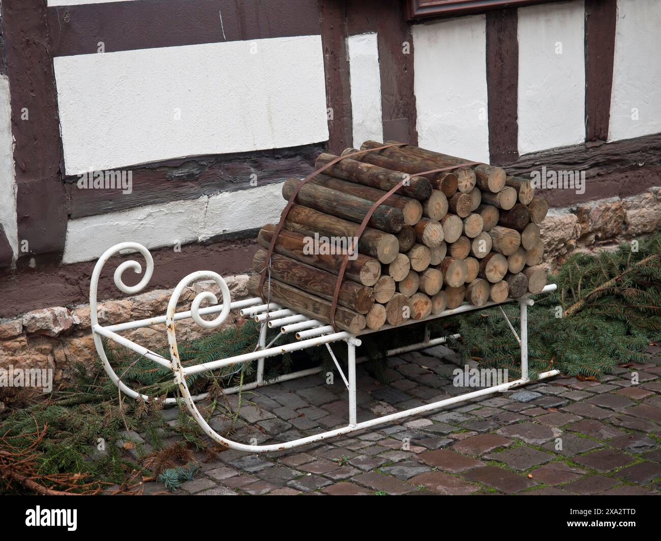 A pile of wood on a white metal sledge in front of an old half-timbered ...