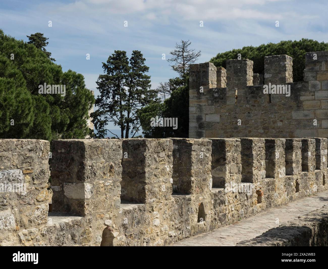 Stone wall of a historic fortress with battlements against a wooded ...