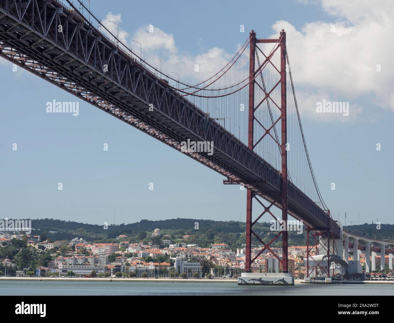 Red steel bridge overlooks a coastal city with blue sky and clouds ...