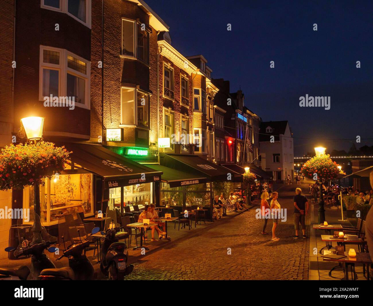 Lively night-time street scene with illuminated buildings, people on ...