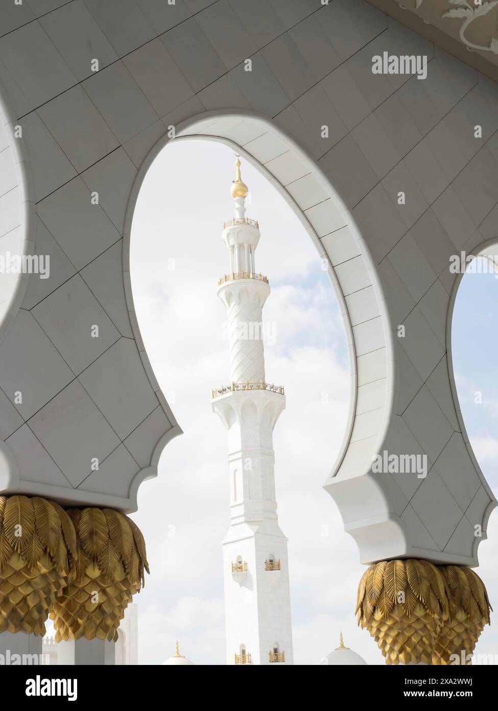 An impressive minaret of a mosque in bright white with golden details ...