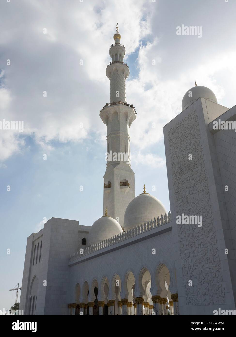 Detailed minaret and parts of a white mosque, shining under a sky with ...