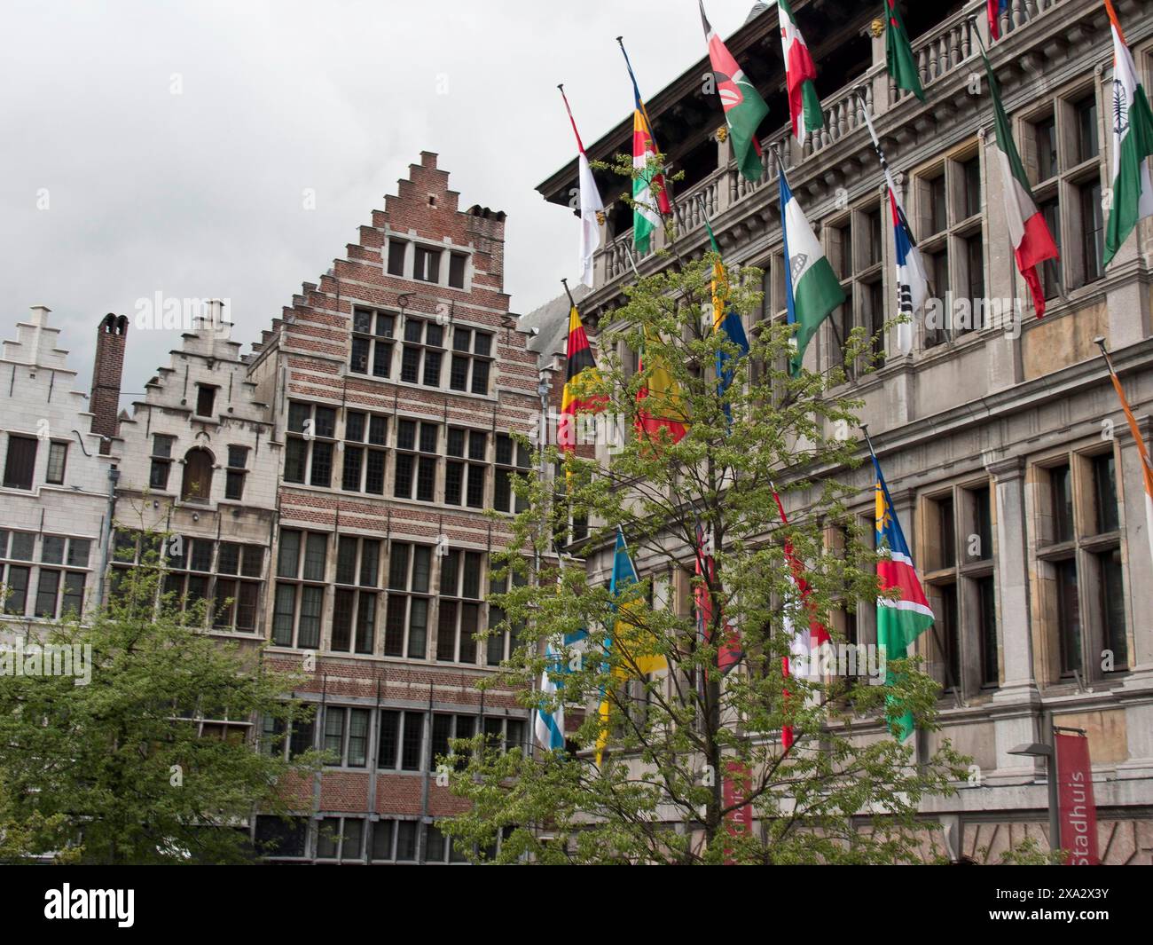 Historic buildings with ornate gables and many flags, trees in front ...