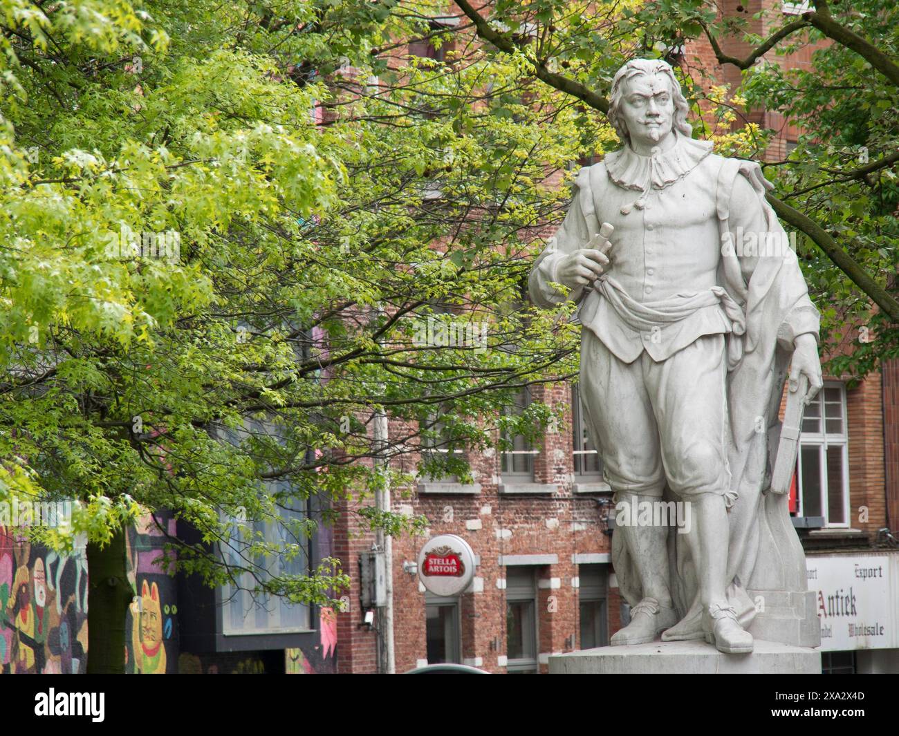 Stone statue of a man in historical clothes in a city park with trees ...