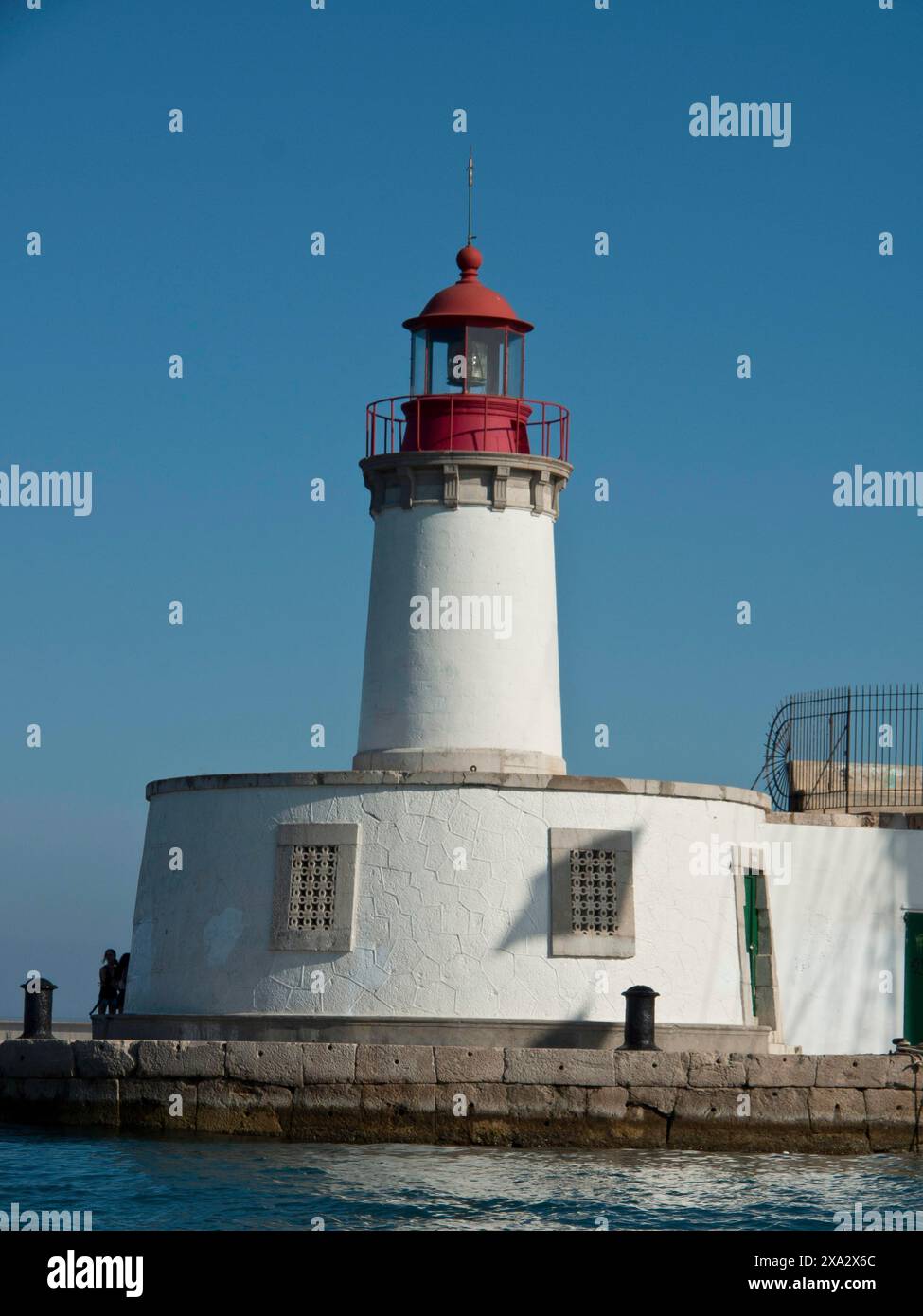 A coastal lighthouse with a red roof and white facade against a blue ...