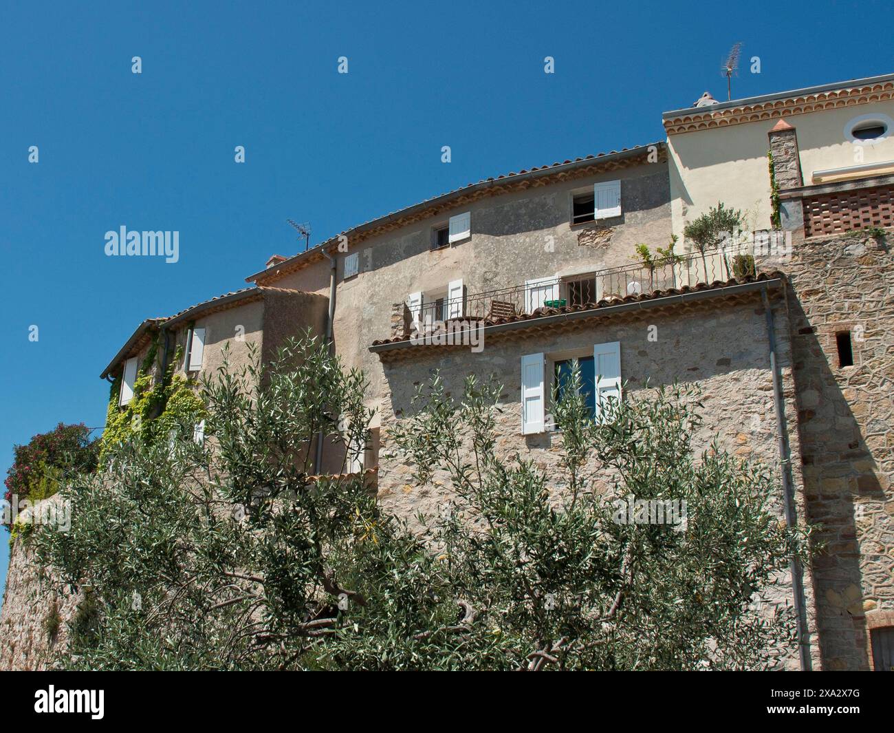 Rustic stone houses with white shutters and vegetation against a clear ...