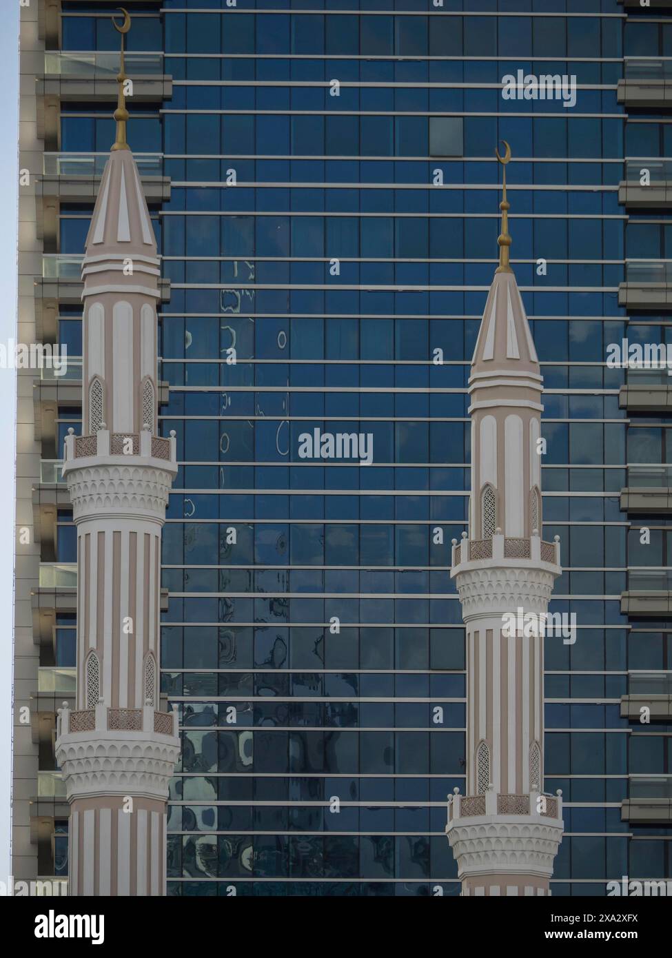 Two minarets of a mosque in front of a modern building with glass ...