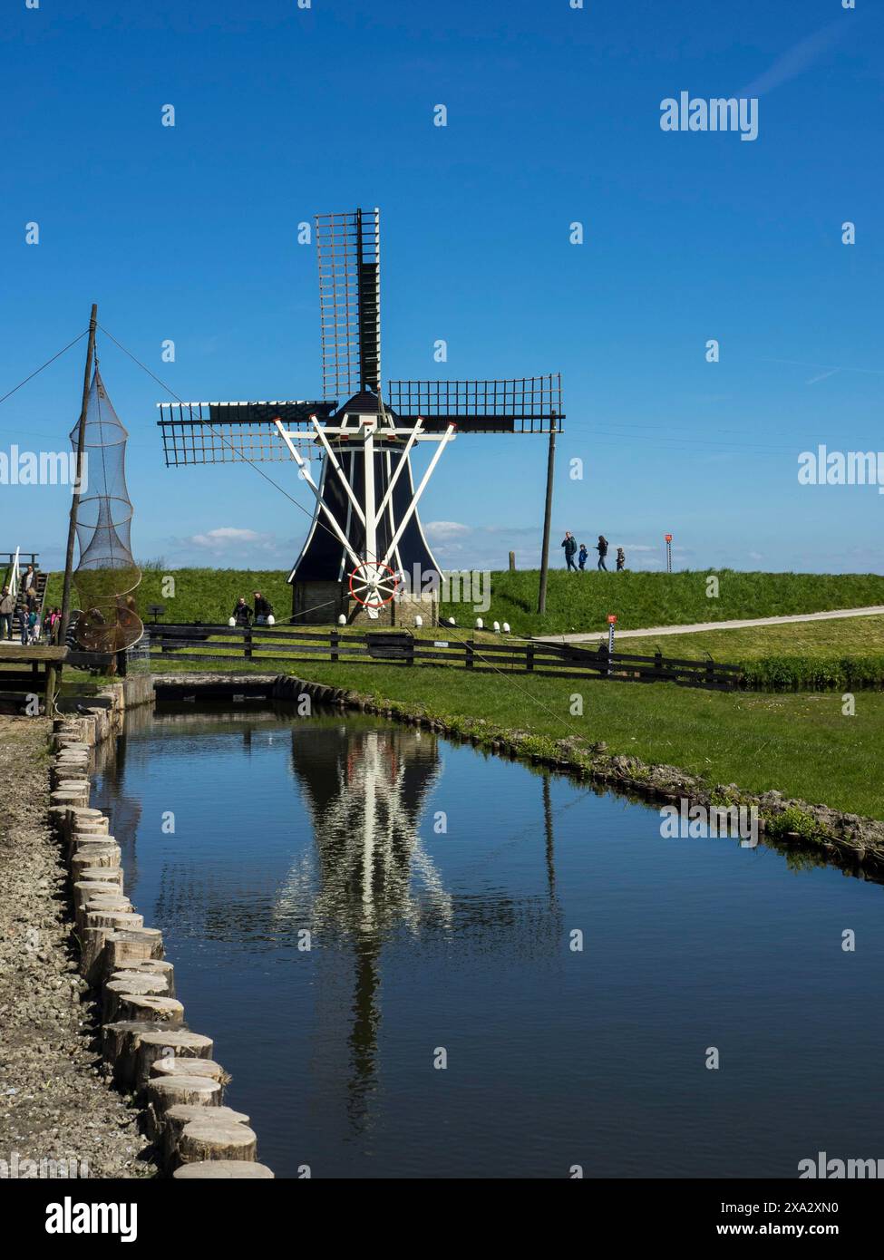 Large windmill with its reflection in a pond, surrounded by people ...