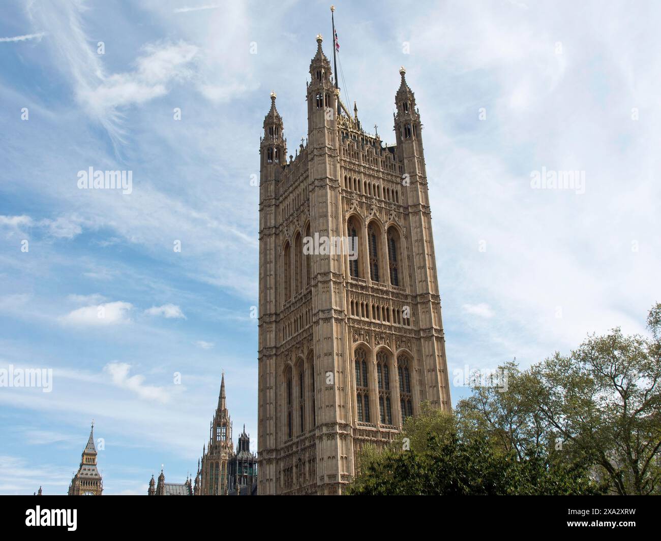Gothic tower rises into the blue sky, surrounded by trees, peaceful ...