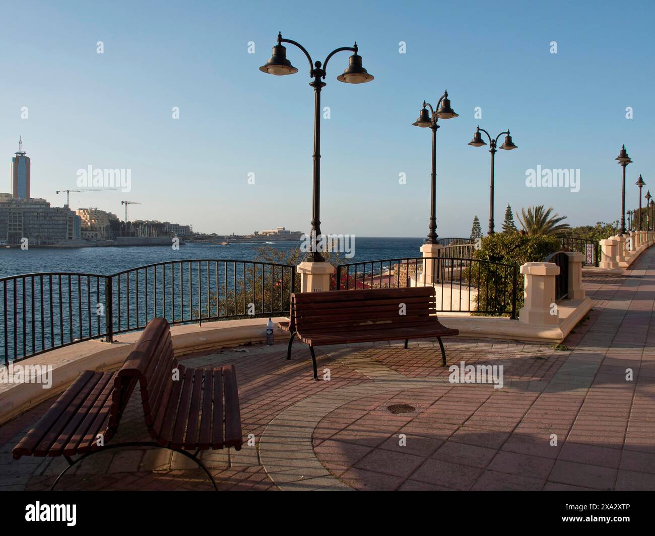 Seafront promenade with benches and decorative lamps, paved floor and ...