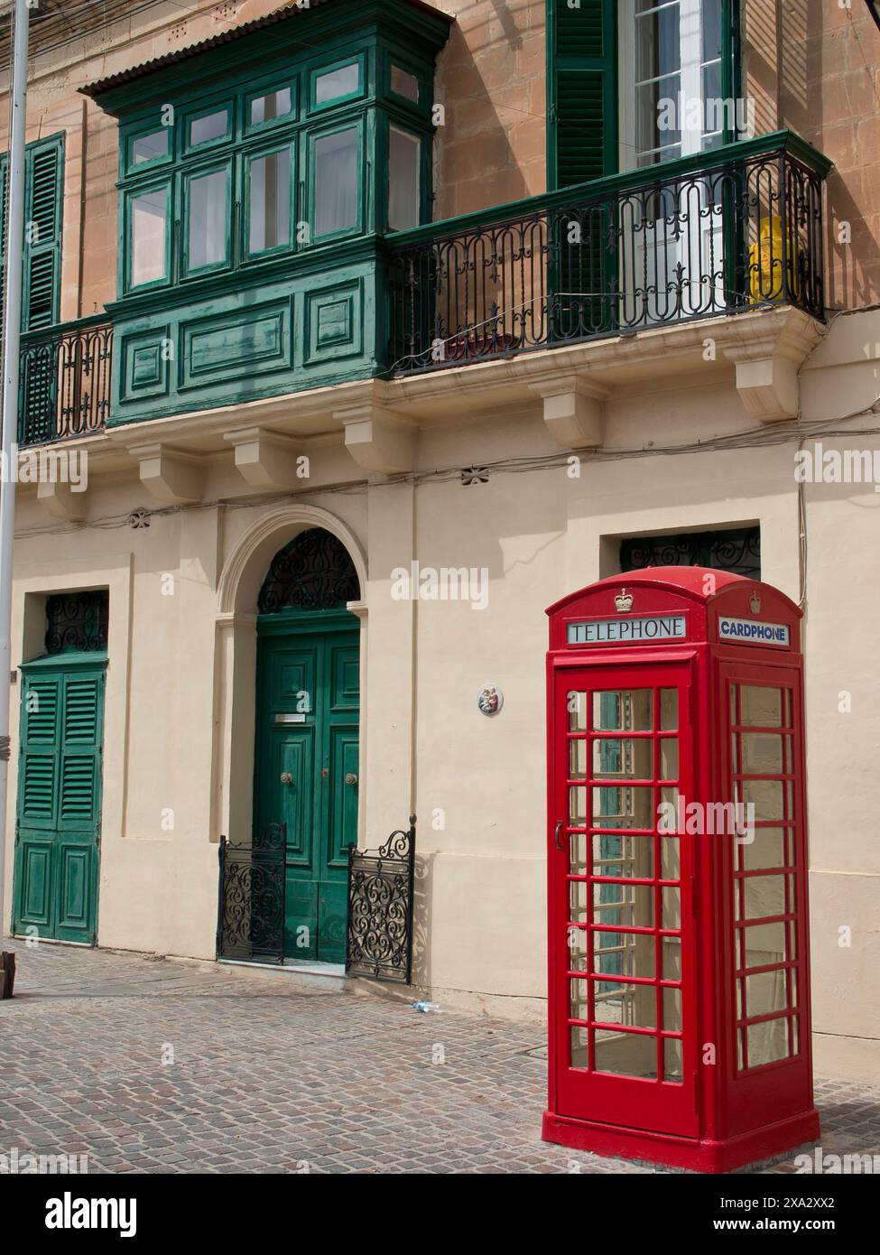 Red telephone box in front of a building with green shutters and ...