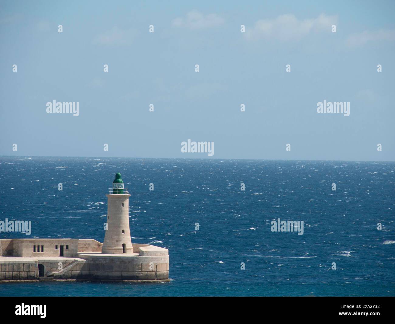 A lighthouse on a pier by the ocean, under a clear blue sky, Valetta ...
