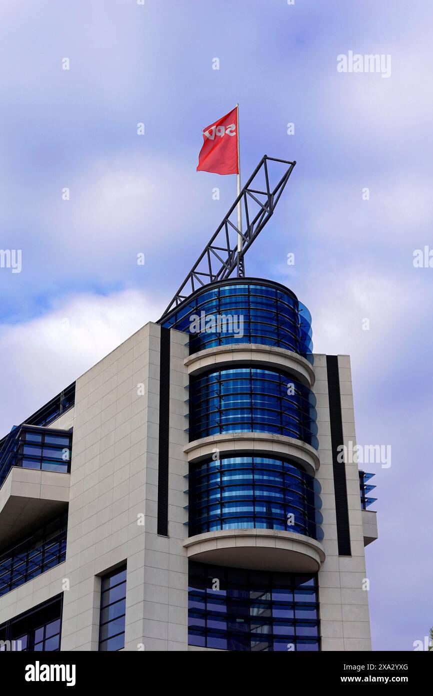 A modern office building with a round glass tower and a flag under a ...