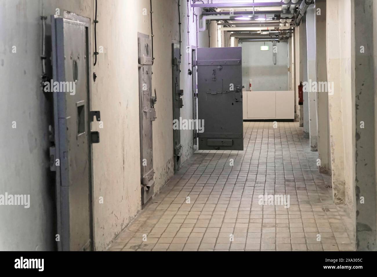 Corridor in a prison with metal cell doors and tiled floor. Gloomy and ...