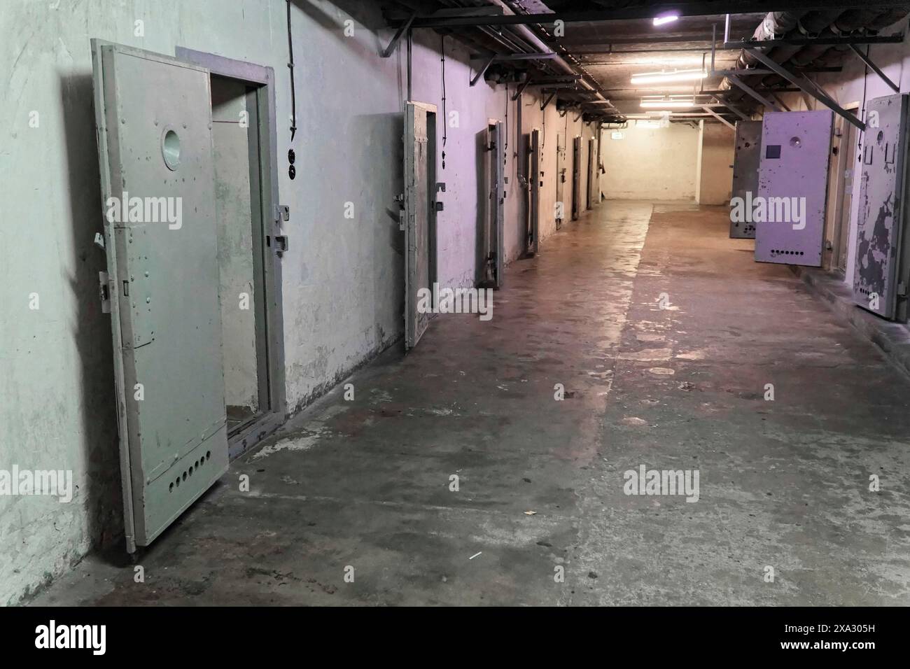 Long prison corridor with several open metal cell doors. Gloomy and ...