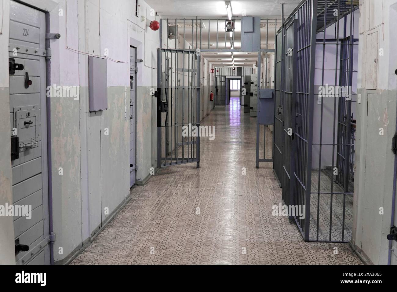 Long corridor of a prison with metal and barred doors and worn walls ...