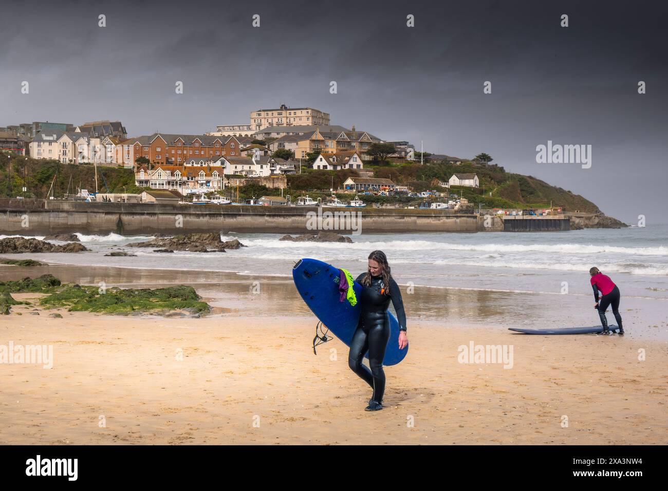 A female surfer carrying her surfboard after surfing at Towan Beach in ...