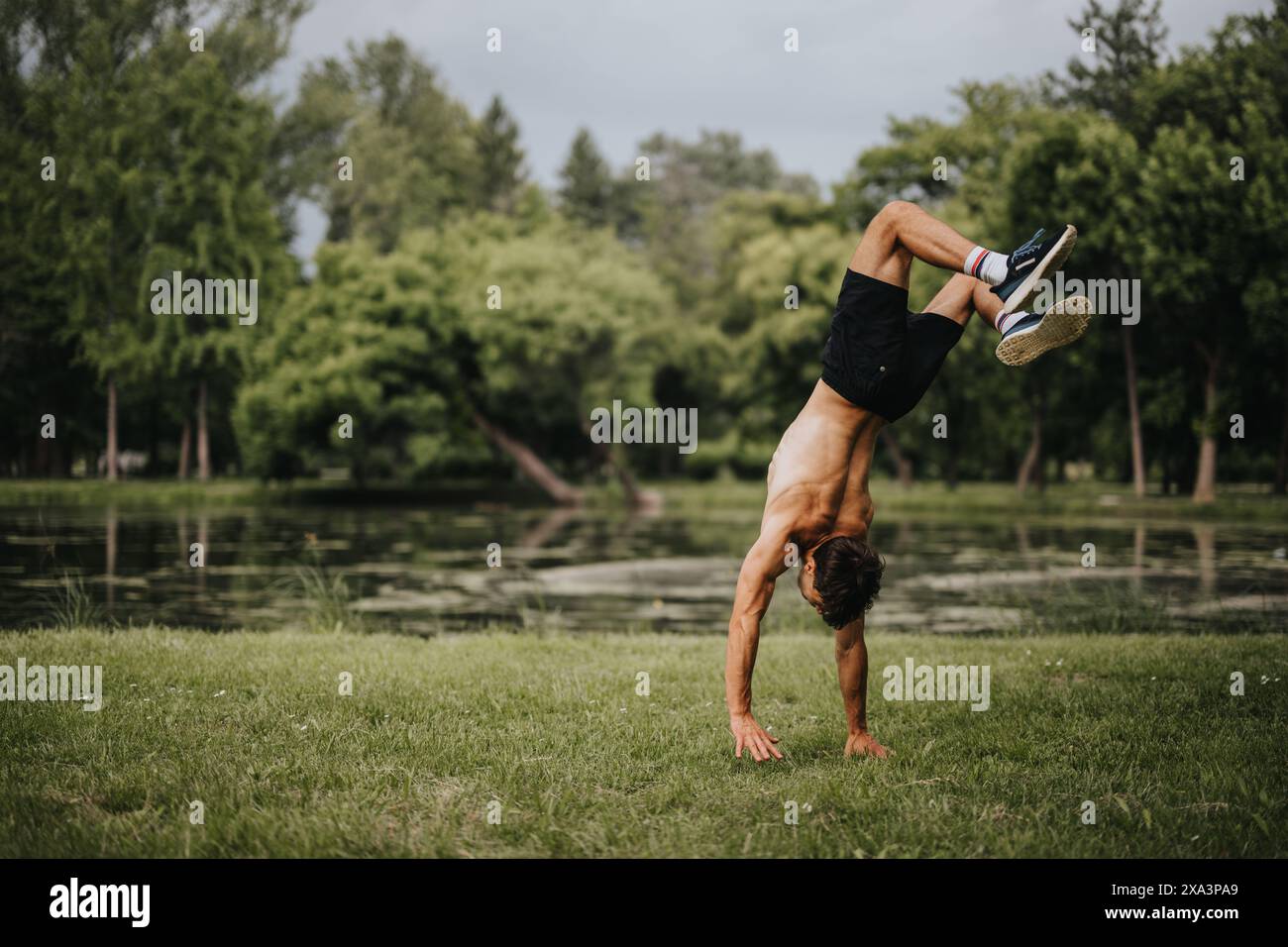 Flexible man performing back flip in a park near a lake on a summer day ...