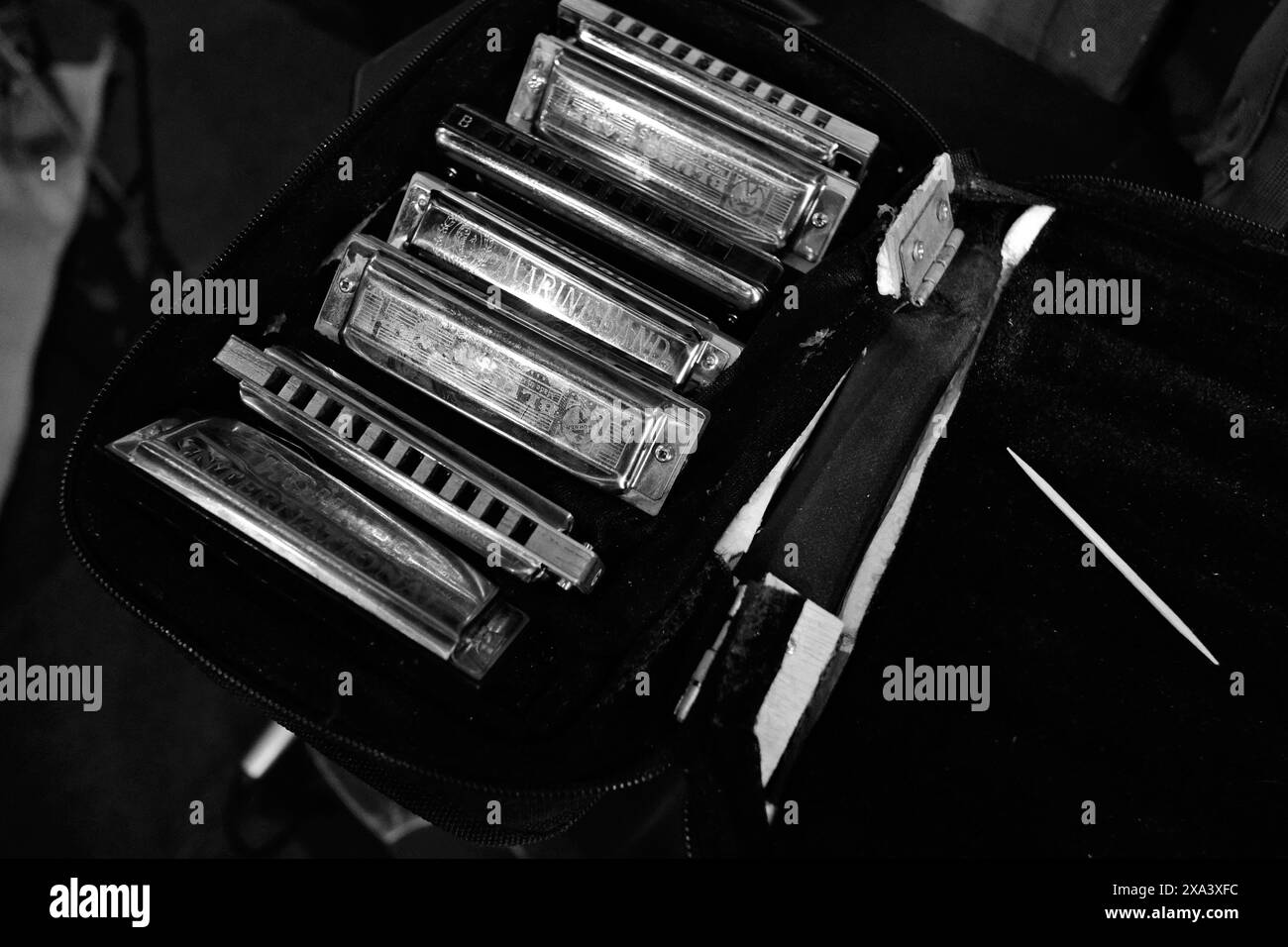 A collection of seven silver harmonicas on stage in a black case ...