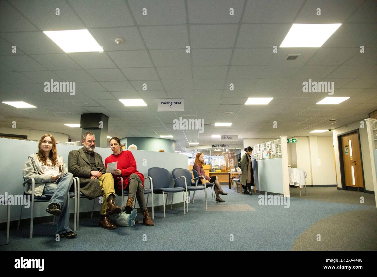 People sitting in a waiting room with chairs and a reception area ...