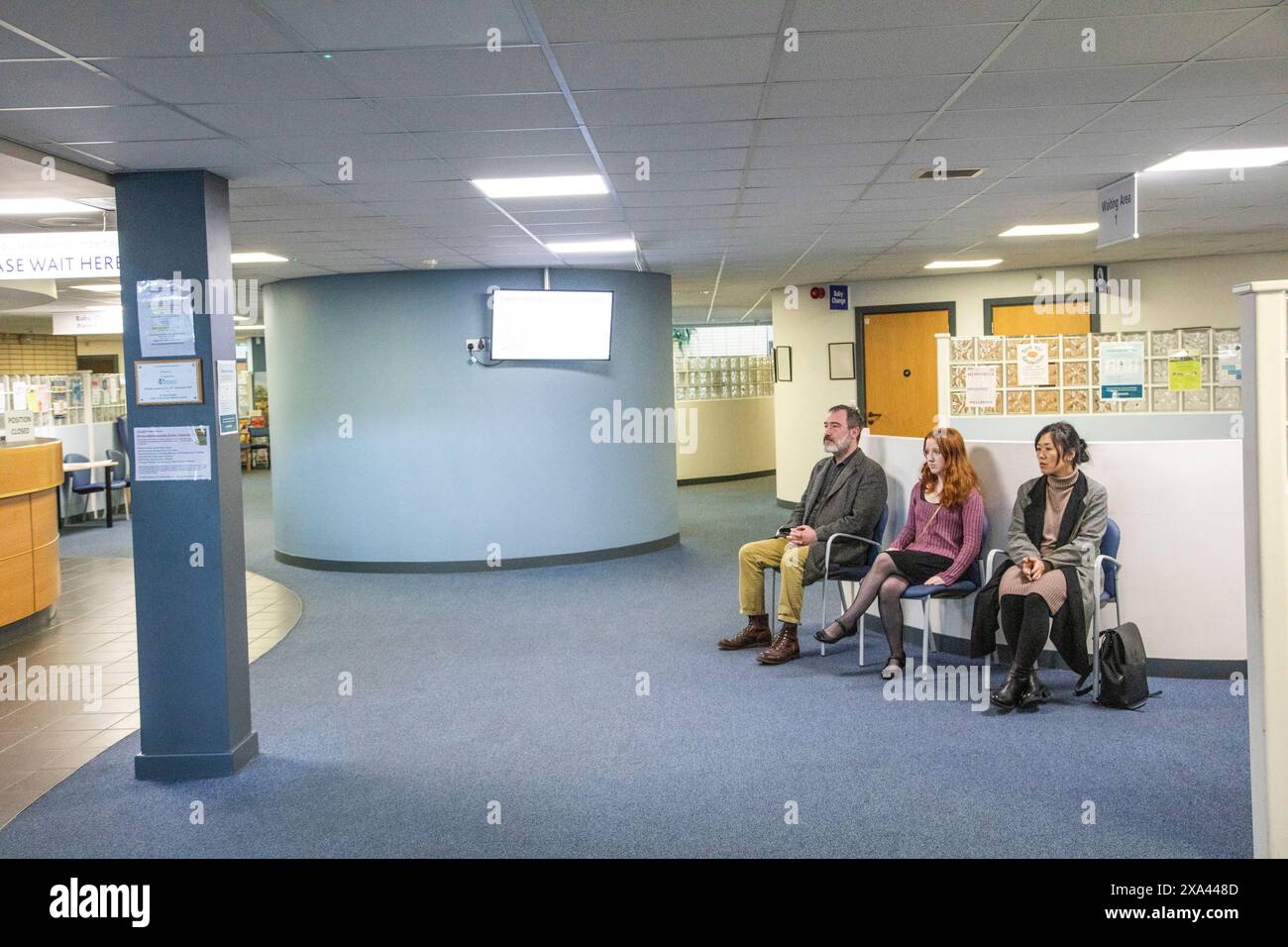 Three people waiting in a modern reception area of a medical practice ...