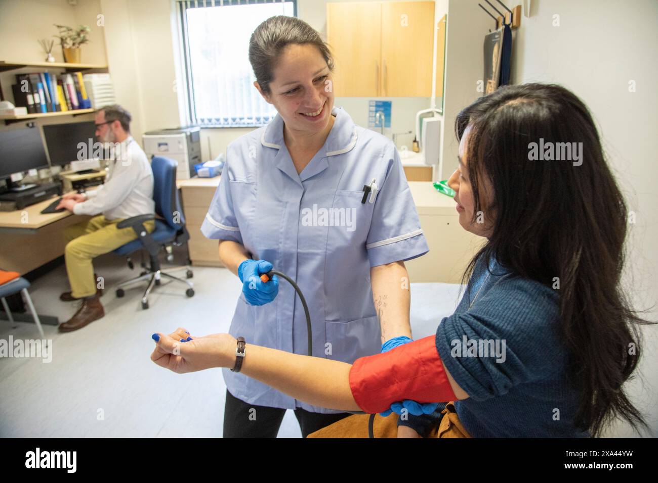 Nurse taking patient's blood pressure in a clinic, doctor in background ...