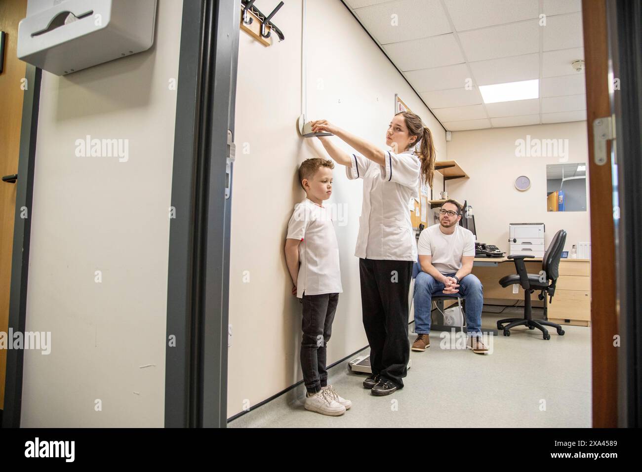 Child being measured during a medical check-up as father observes Stock ...