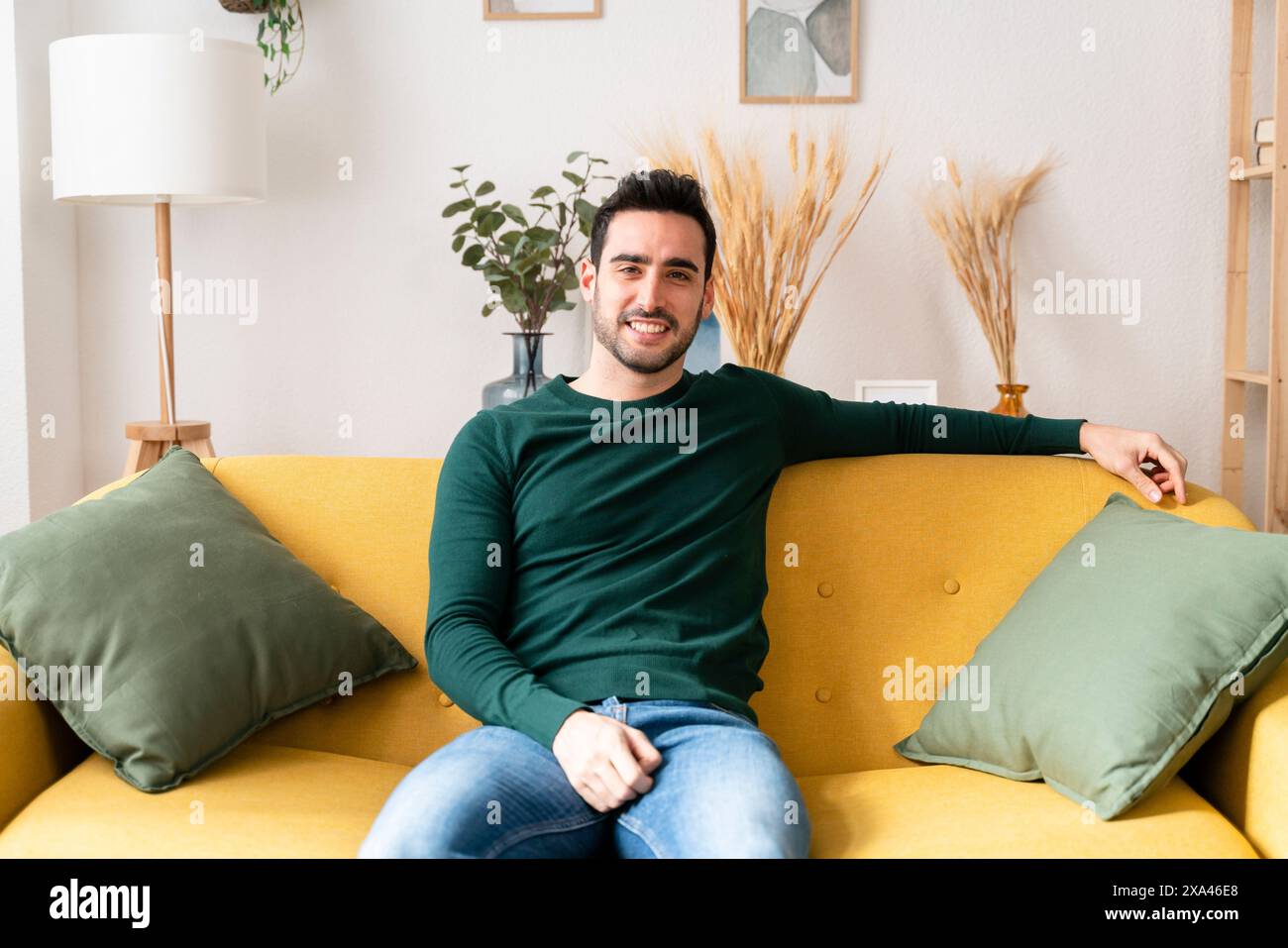 Smiling man sitting comfortably on a yellow couch Stock Photo - Alamy